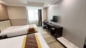 Quarto de hotel com duas camas, uma escrivaninha, uma cadeira, uma televisão e uma janela com cortinas.