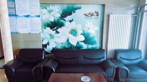 Uma área de recepção com um sofá marrom escuro, uma mesa de centro de madeira e uma grande pintura floral na parede.