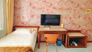 Quarto de hotel com cama, escrivaninha com televisão, cadeira e armário para sapatos.