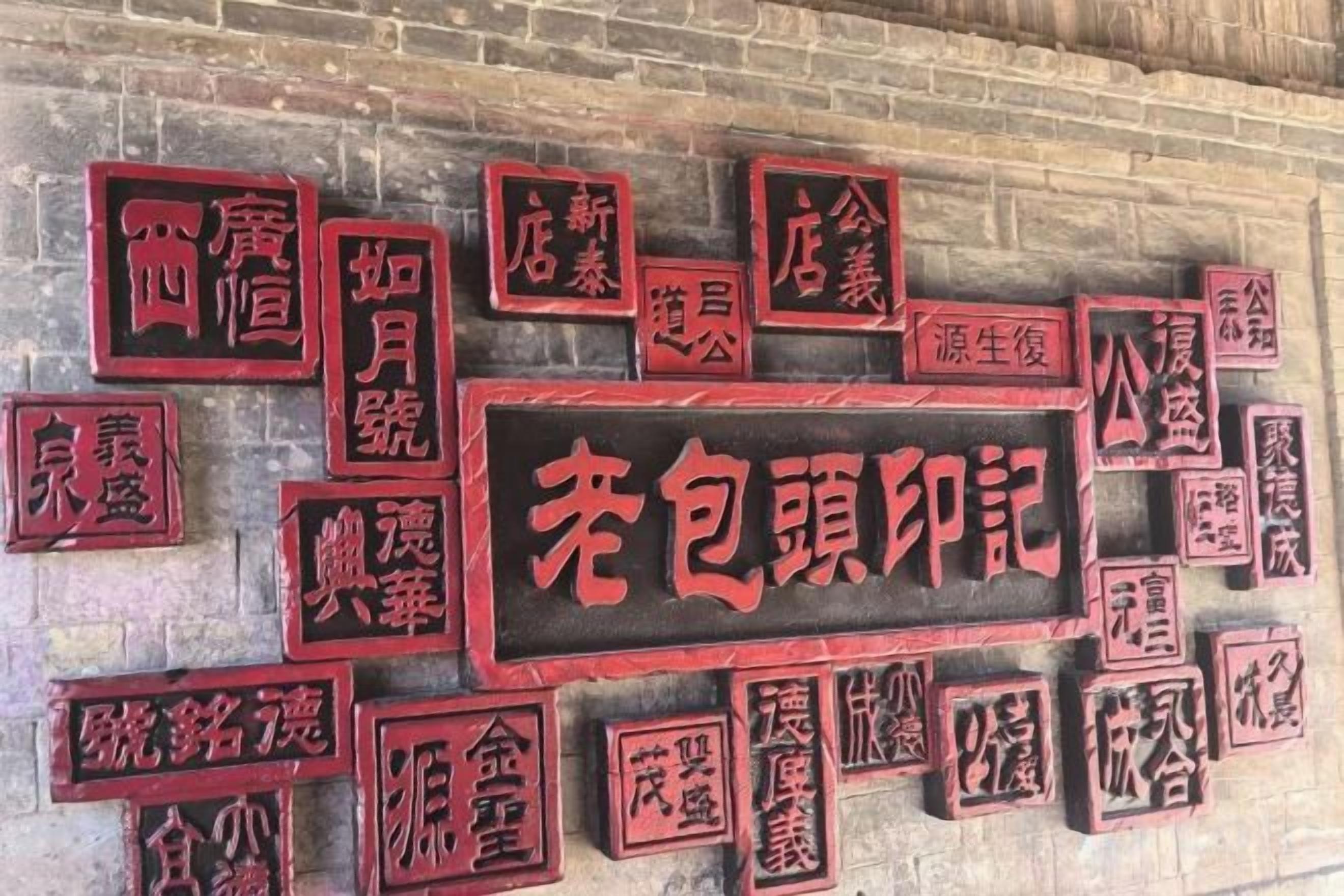 Uma parede com várias placas retangulares vermelhas com caracteres chineses, algumas com texto branco adicional.