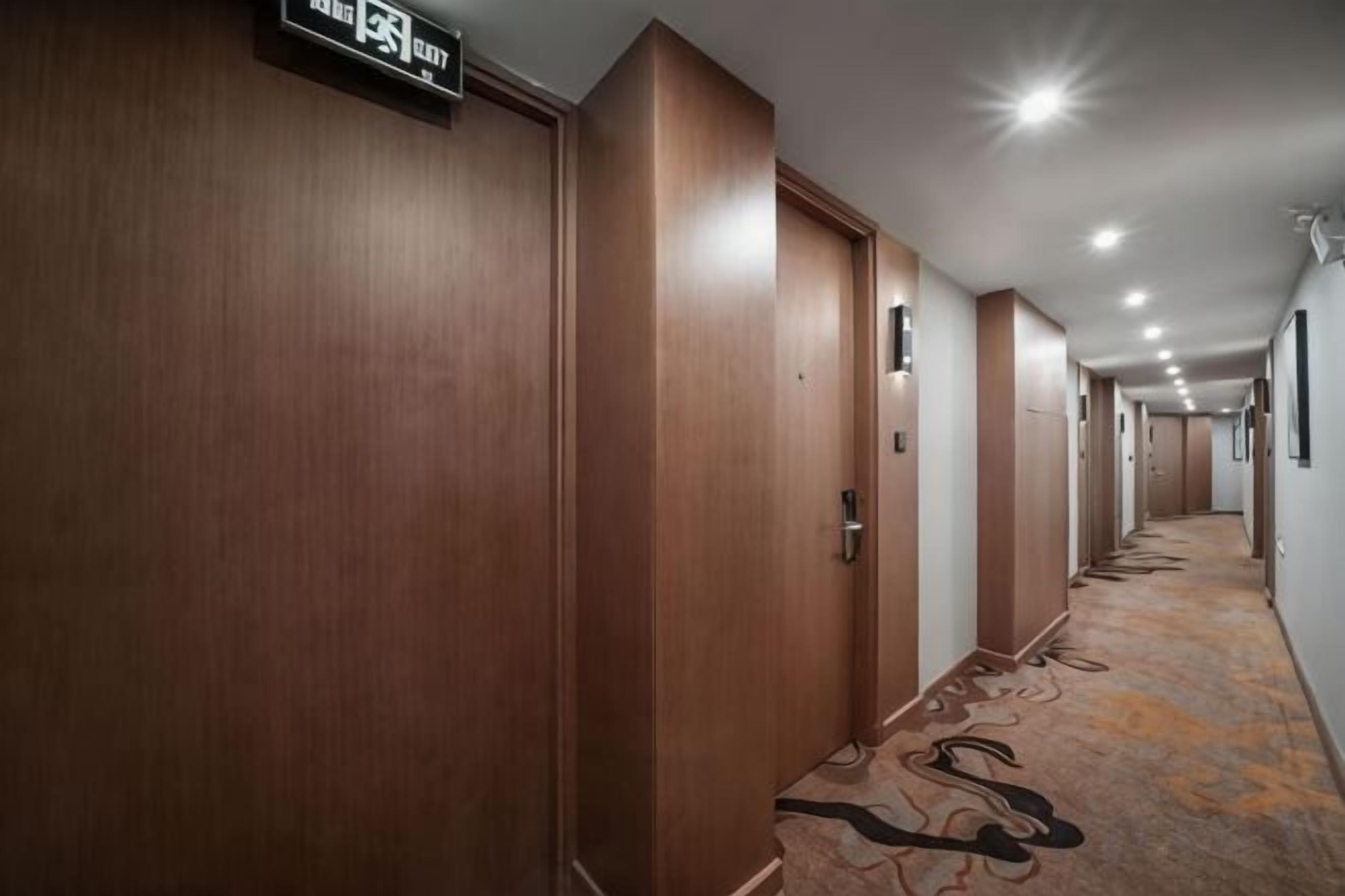 Corredor de hotel com portas de madeira, piso coberto por carpete e iluminação embutida.
