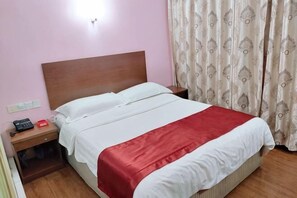 Uma cama de solteiro com cabeceira de madeira, mesa de cabeceira com um telefone e um objeto vermelho, e cortina estampada.