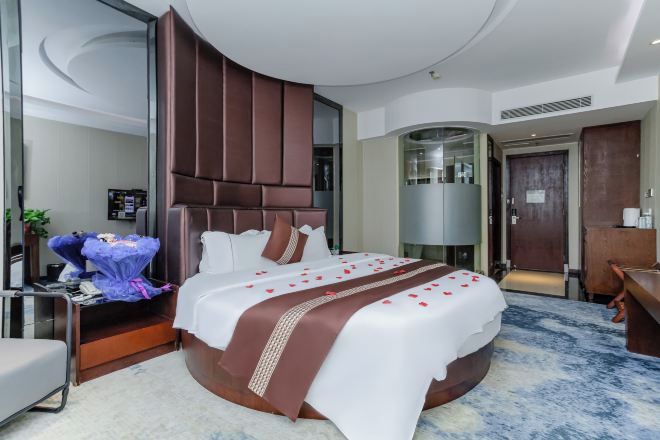 Quarto de hotel moderno com cama curvada, cabeceira grande, mesa de cabeceira e criado-mudo.