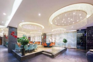 Um lobby de hotel moderno com área de estar central, balcão de recepção e um grande candelabro decorativo.