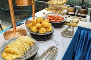 Mesa de buffet com diversos alimentos, incluindo doces, cachorros-quentes e um espaço para bebidas.