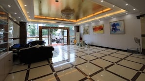 Um saguão de hotel com piso xadrez, um candelabro e obras de arte nas paredes.