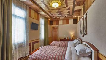 Quarto de hotel com duas camas, teto de madeira e uma janela grande com cortinas.
