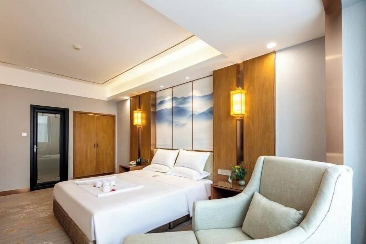 Quarto de hotel com cama, duas mesas de cabeceira, uma cadeira e um guarda-roupa.