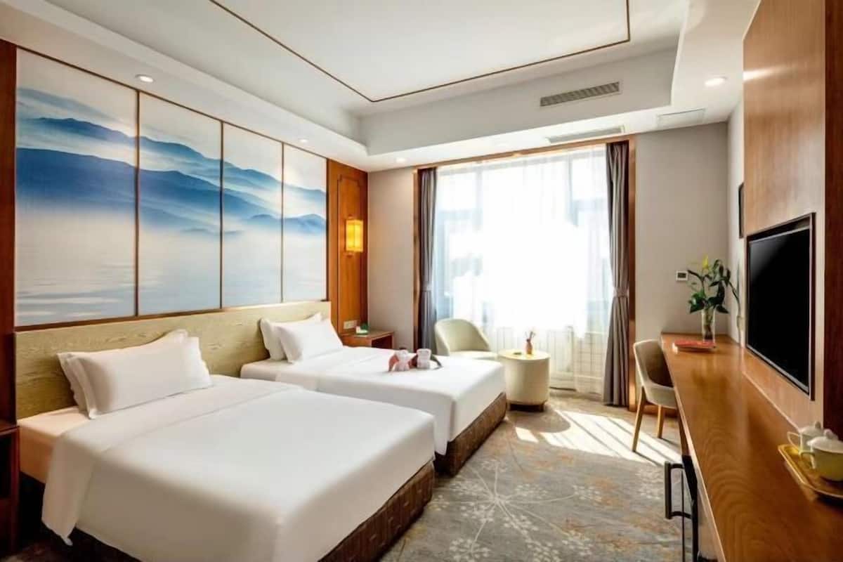Quarto de hotel com duas camas, uma mesa, uma televisão e uma janela grande.