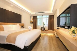 Quarto de hotel com uma cama grande, televisão de tela plana, mesinha e um vaso com flores.