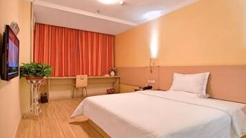 Quarto de hotel com cama, escrivaninha, cadeira, planta e janela com cortinas.