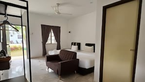 Quarto de hotel com cama, uma cadeira, escrivaninha, espelho, ventilador de teto e porta.