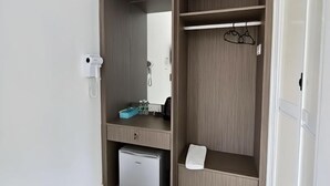 Quarto compacto com roupeiro embutido, um pequeno frigorífico, espelho e porta-toalhas.