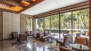 Um espaço interno amplo, com piso lustroso, diversos conjuntos de assentos e grandes janelas que oferecem vista para o verde lá fora.