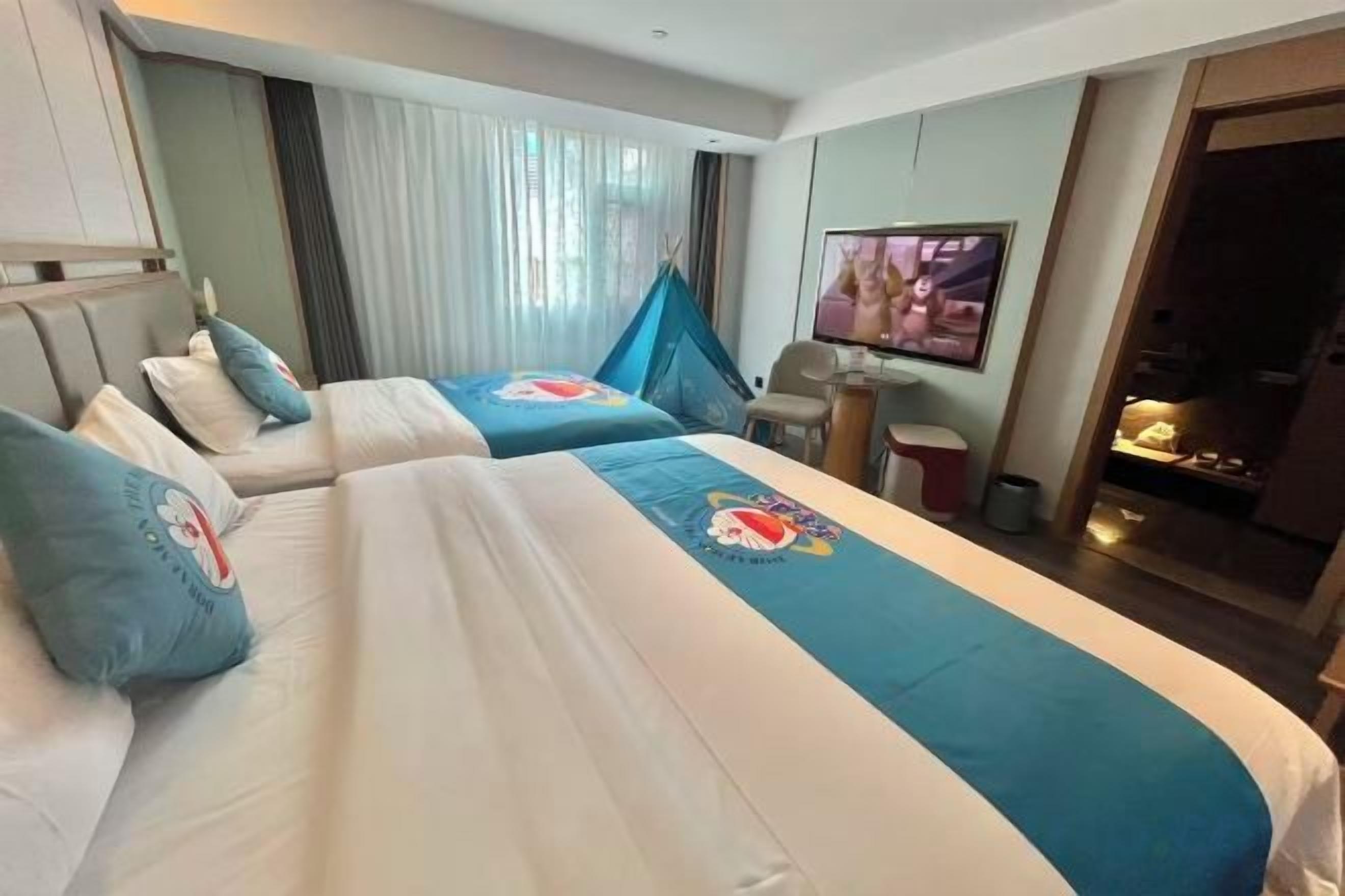 Quarto de hotel com duas camas, televisão, escrivaninha e janela com cortinas.