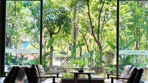 Quarto com uma janela ampla, duas cadeiras, uma mesa pequena e vista para o verde lá fora.