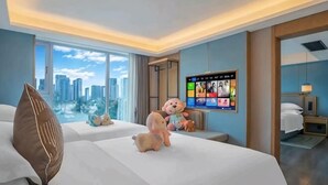 Quarto de hotel com uma janela grande, TV de tela plana e brinquedos macios na cama.