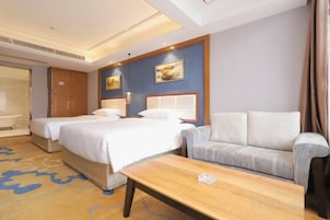 Quarto de hotel com duas camas, um sofá, uma mesa de madeira e banheiro com banheira.