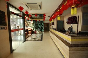 Um saguão de hotel com balcão de recepção, parede estampada e lanternas vermelhas.