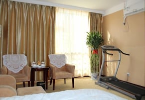 Quarto de hotel com cama, duas cadeiras, uma mesinha com objetos, esteira e um vaso de planta.