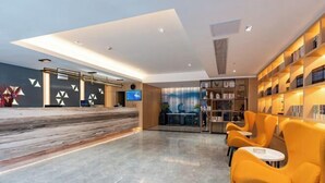 Um hall moderno com piso de mármore, balcão de recepção, televisão e área de estar com cadeiras amarelas.