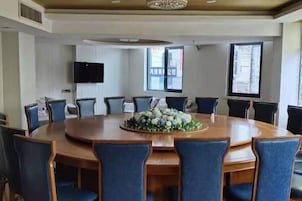 Sala de conferências com mesa redonda, cadeiras azuis e um arranjo floral.