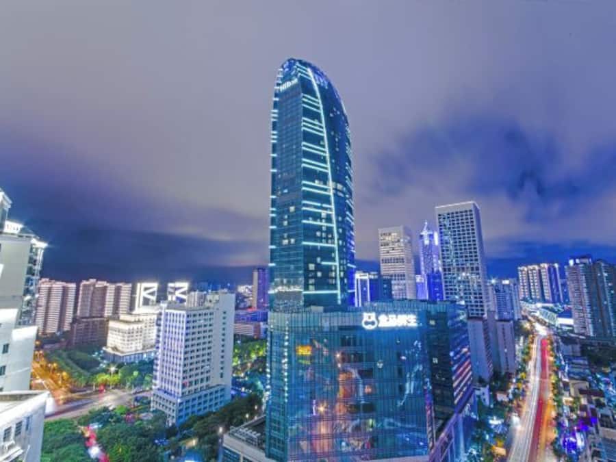 Paisagem urbana com edifícios modernos altos, incluindo um arranha-céu curvo com sinalização iluminada.