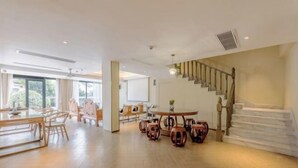 Uma sala de estar ampla com piso de madeira, uma mesa de jantar com cadeiras, uma escada e uma grande janela que oferece iluminação natural.