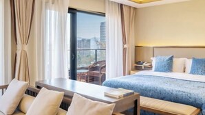 Quarto de hotel com cama, escrivaninha, cadeira e vista da cidade.