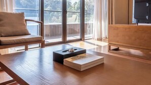 Quarto moderno com uma mesa de madeira, uma cadeira estofada, uma mesinha com caixa de lenços, um armário de madeira e uma TV fixada na parede.