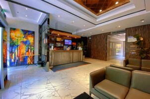 Um hall de hotel com balcão de recepção, área de estar e uma grande pintura abstrata.