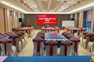 Uma sala de conferências com fileiras de cadeiras, uma tela grande e um pódio.
