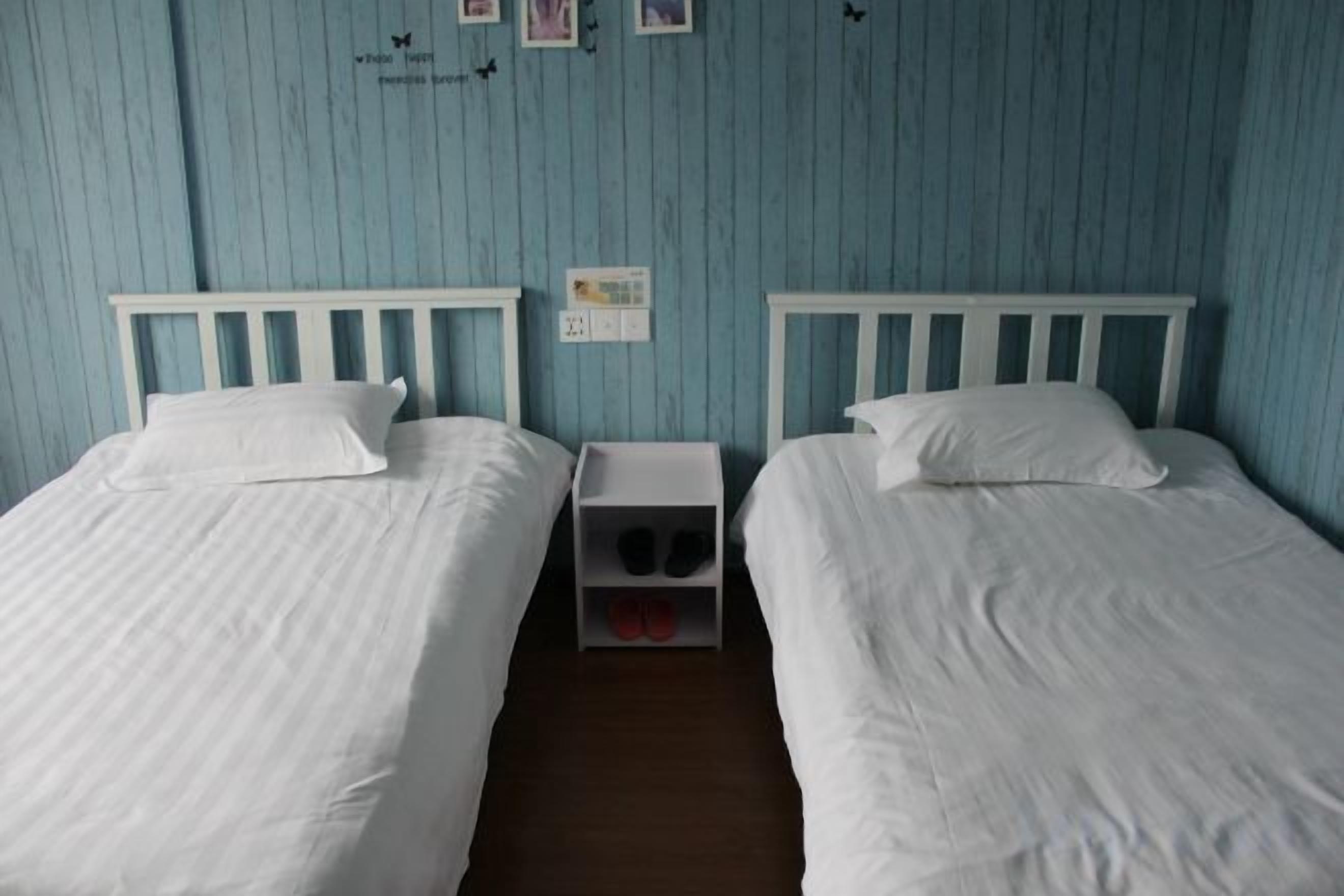 Quarto com duas camas de solteiro, mesa de cabeceira com abajur e tomada na parede.