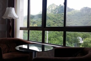 Um quarto com uma grande janela, uma mesa de vidro redonda e duas poltronas marrons.