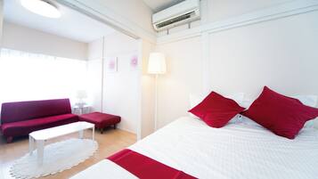 Quarto de hotel com uma cama, um sofá vermelho, uma mesa branca e um abajur branco.