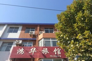 Um edifício com toldo vermelho exibindo o nome '鸿华旅馆' e um número de telefone.