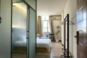 Quarto de hotel com cama, escrivaninha, cadeira, planta em vaso e porta de correr.