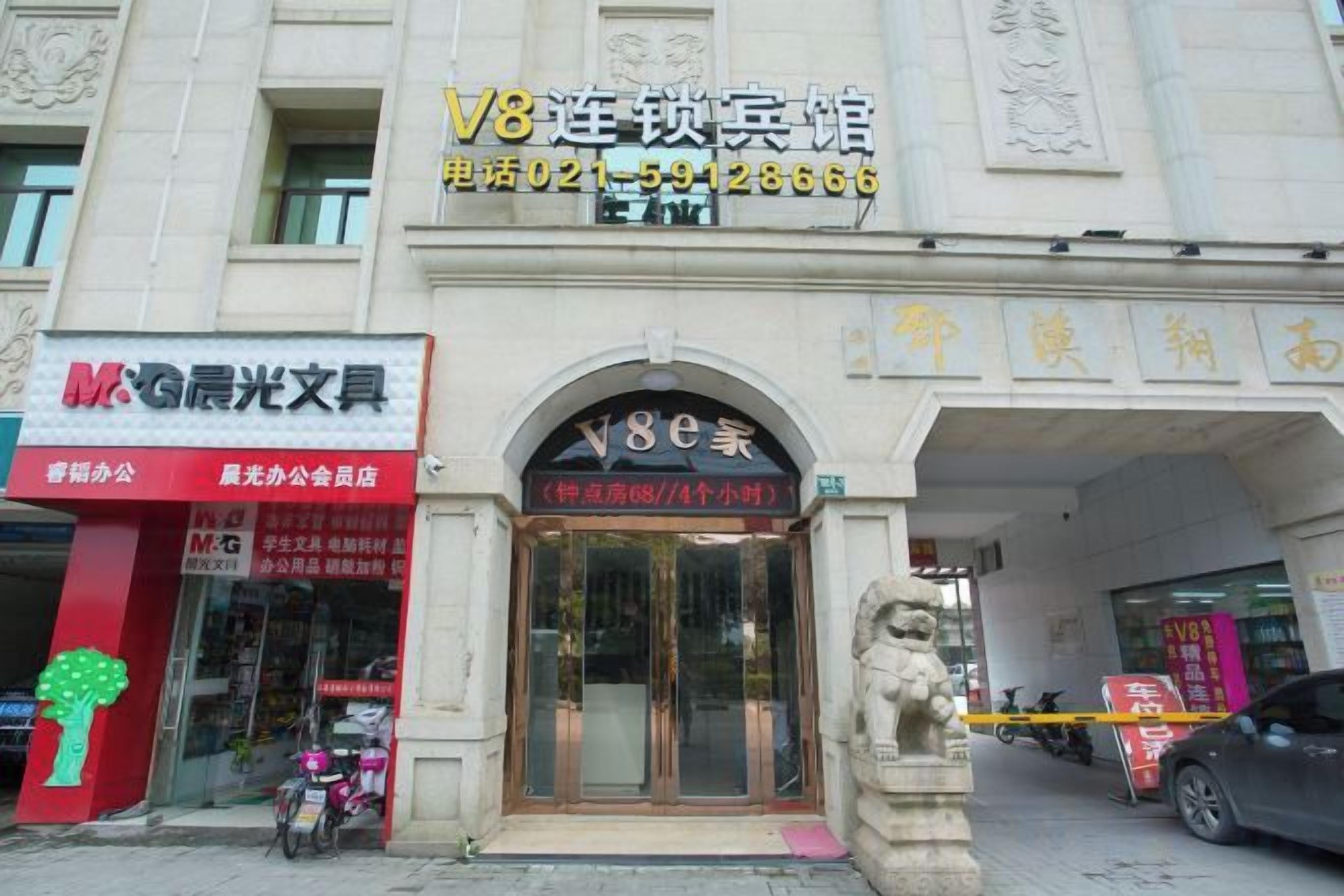 Um edifício com fachada exibindo a inscrição 'V8连锁宾馆' e um letreiro para 'M&G晨光文具'.
