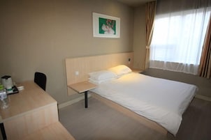 Quarto de hotel com cama, escrivaninha, cadeira, um quadro na parede e janela com cortinas.