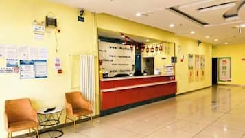 Uma área de recepção com balcão vermelho, duas cadeiras e piso de azulejos.