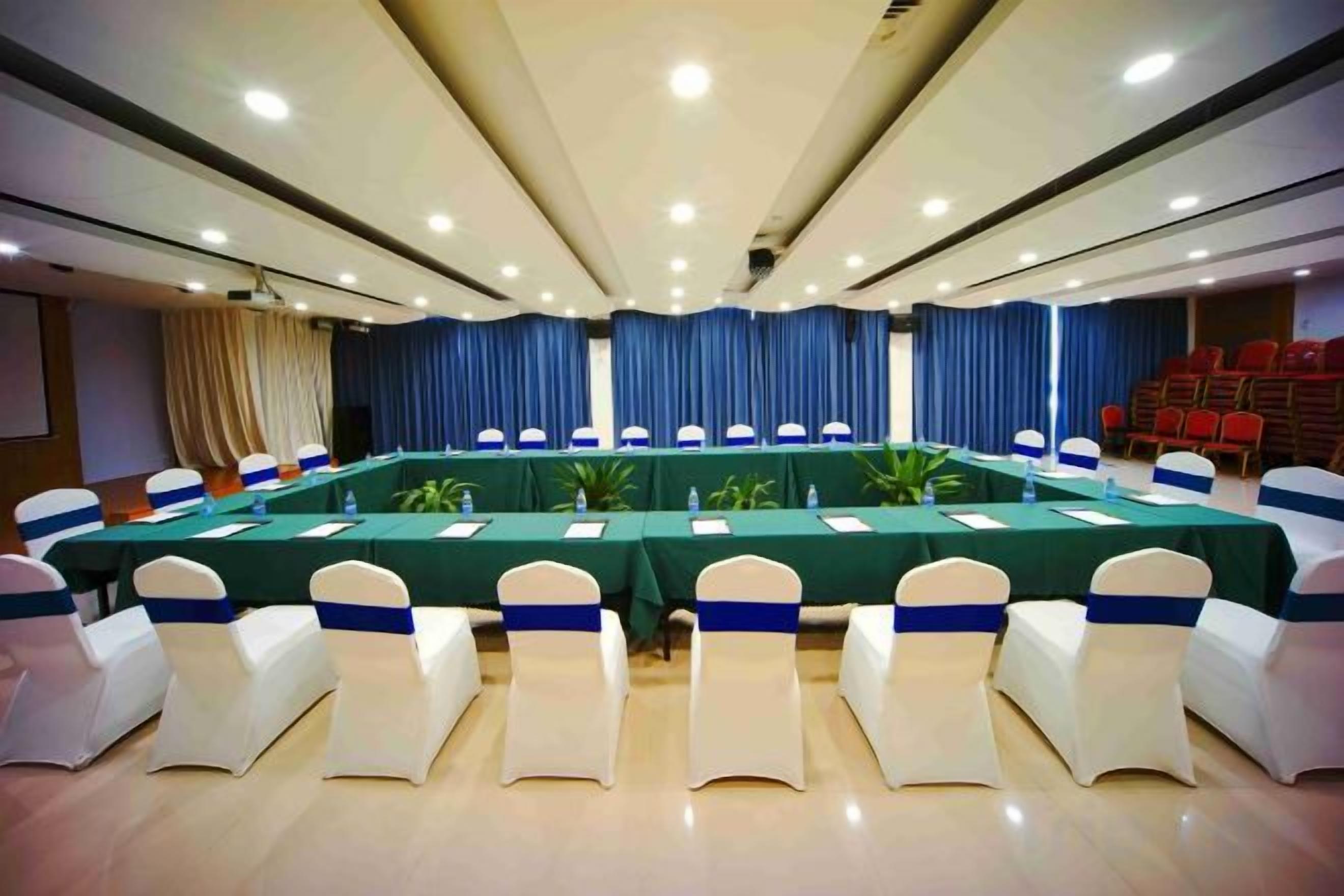 Sala de conferência com uma mesa comprida, cadeiras com fitas azuis e um fundo de cortina azul.