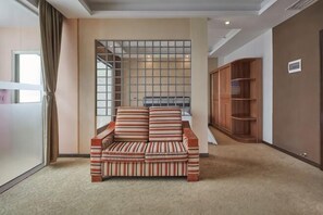 Um quarto com um sofá listrado, uma janela grande com cortinas, uma estante de livros e uma porta.