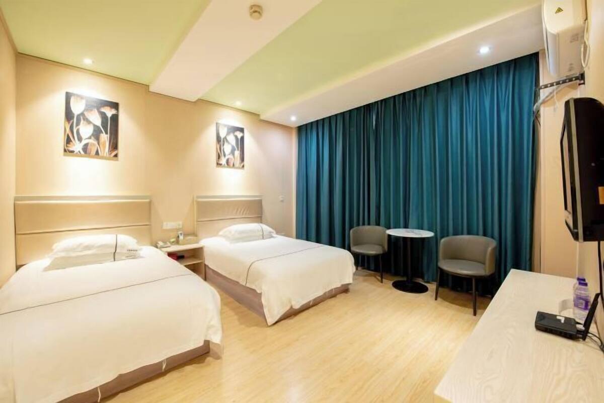 Quarto de hotel com duas camas, uma escrivaninha, uma cadeira, televisão e obras de arte nas paredes.