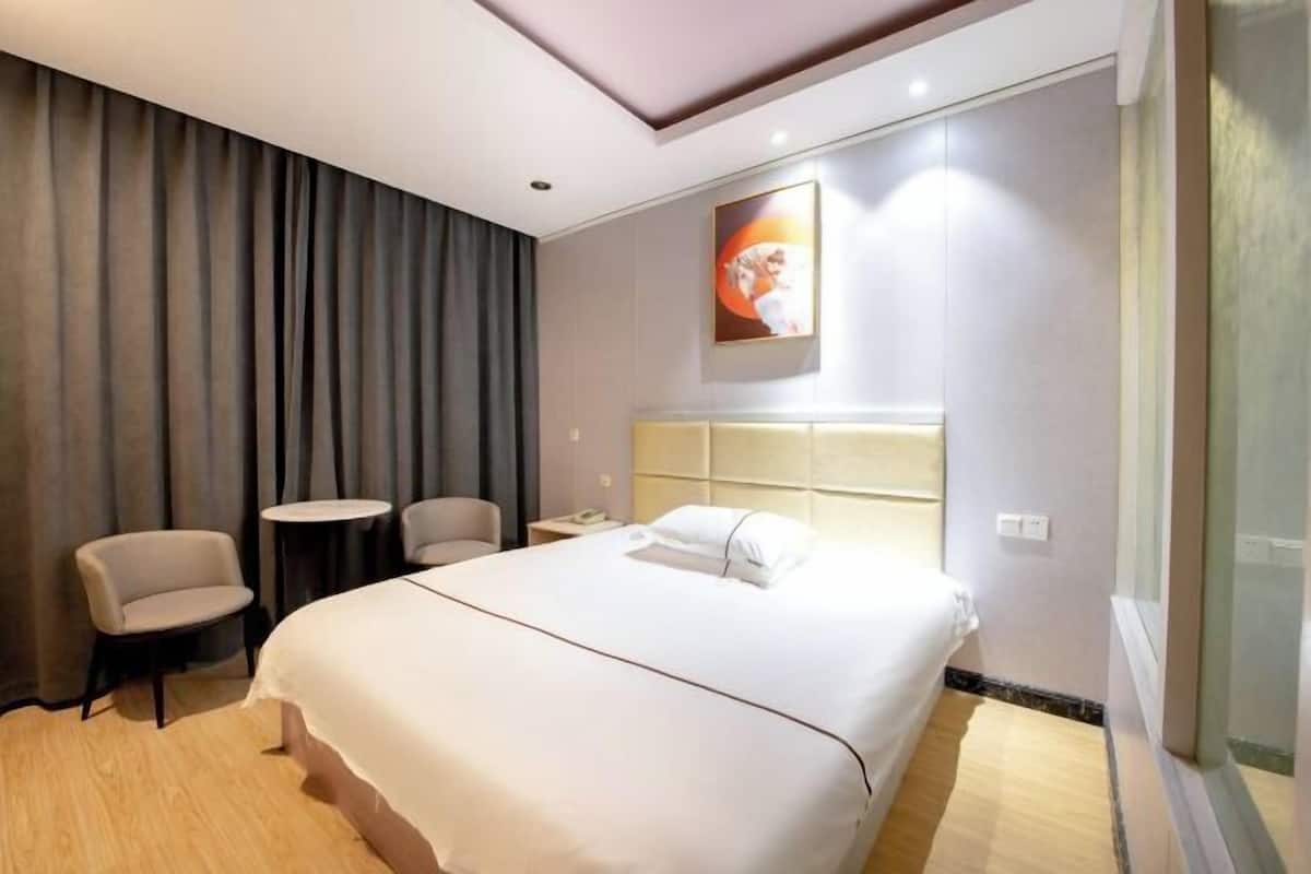 Quarto de hotel moderno com uma cama grande, duas cadeiras, uma mesinha e um quadro na parede.