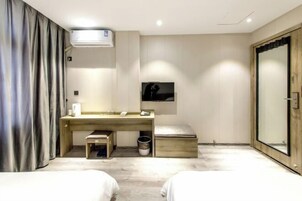 Quarto de hotel com uma cama, escrivaninha, cadeira, mesa pequena, lixeira, espelho e televisão.
