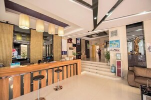 Um saguão moderno de hotel com balcão de recepção, banquetas de bar, escada e um sofá.