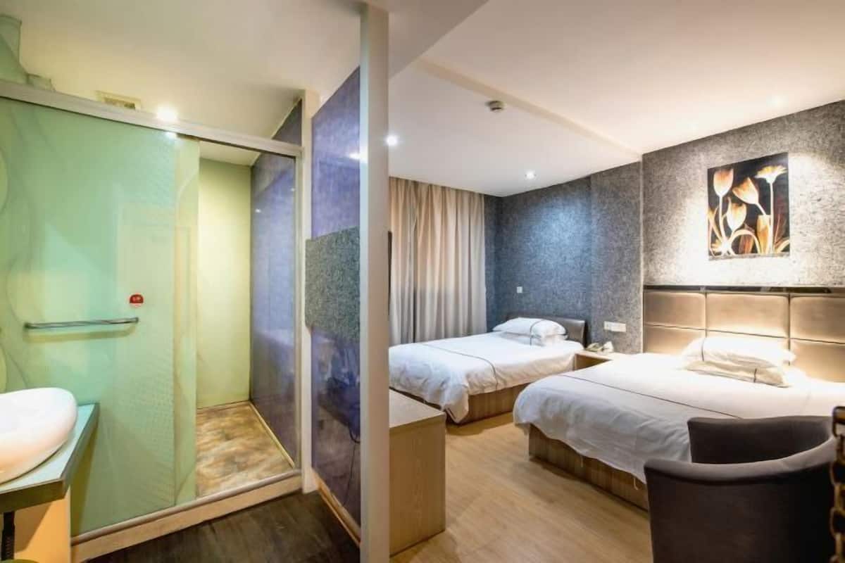 Quarto de hotel com chuveiro de vidro, duas camas individuais, uma secretária pequena e uma cadeira.