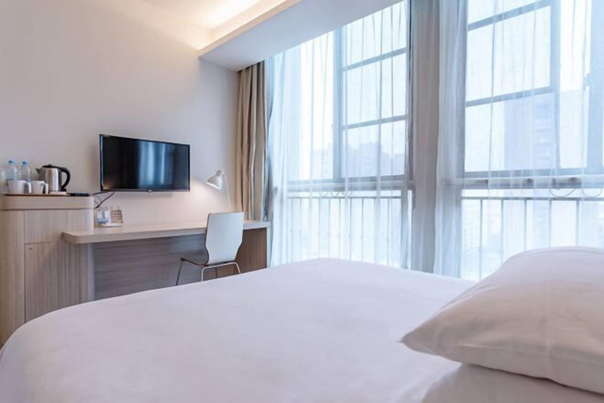 Quarto de hotel com cama, escrivaninha, televisão de tela plana, cadeira e janela com cortinas.