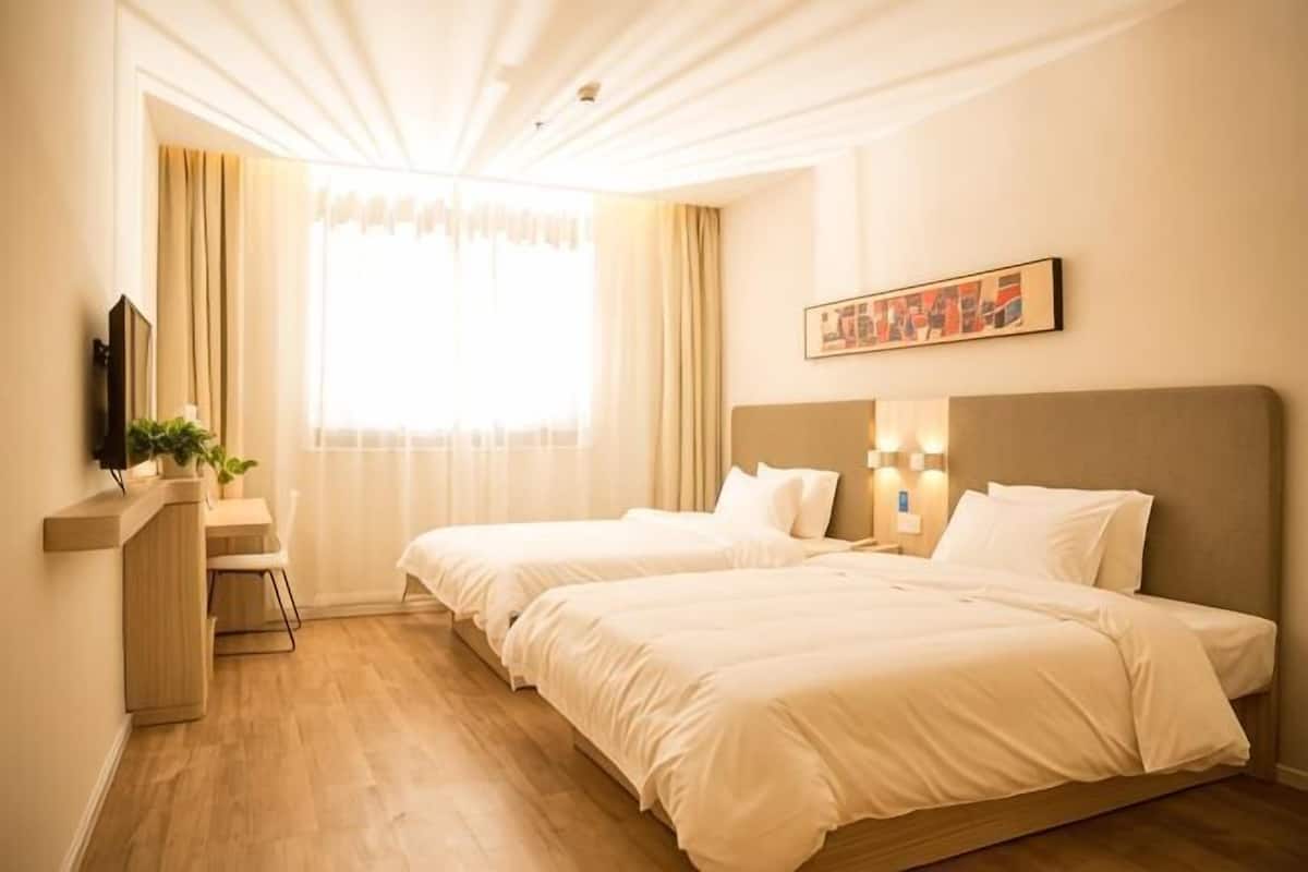 Quarto de hotel com duas camas, uma mesa, uma cadeira, televisão e uma janela com cortinas.