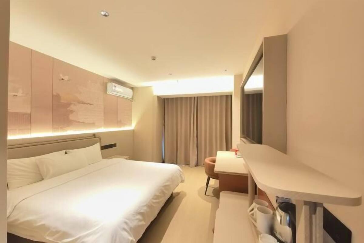 Quarto de hotel com cama, escrivaninha, cadeira, espelho e ar-condicionado fixado na parede.